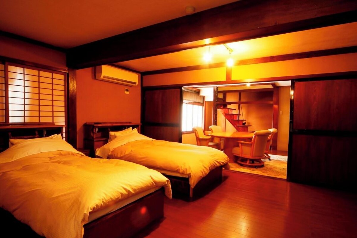 Quarto de hotel com duas camas, área de refeições e escada.