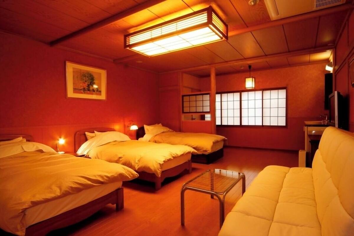 Quarto com três camas, um sofá, uma mesinha e um tradicional separador japonês shoji.