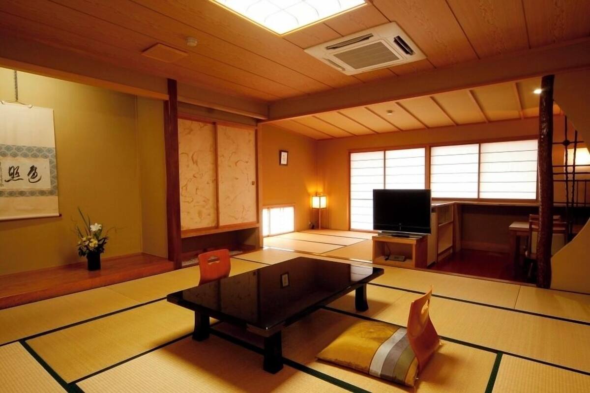 Um quarto com tatames, uma mesa de tatame, uma televisão e um candeeiro de estilo japonês tradicional.