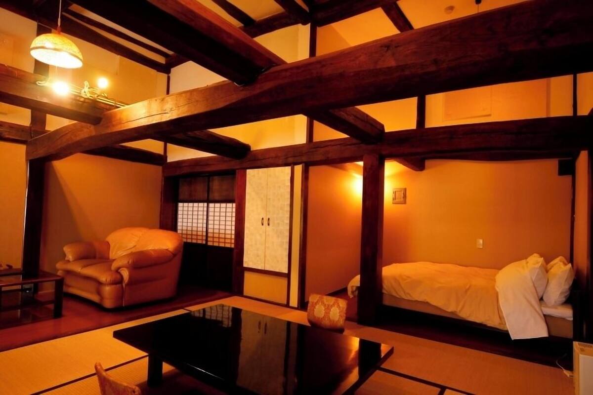 Um quarto japonês tradicional com tatames, uma mesa baixa, um sofá e uma cama.