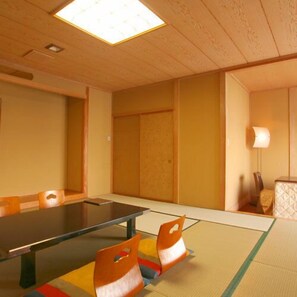 Quarto com piso de tatame, uma mesa baixa e cadeiras laranjas.
