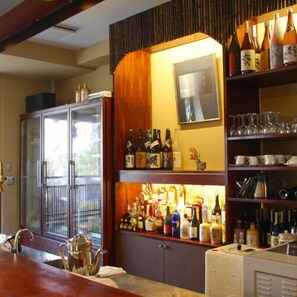 Uma área de bar com prateleiras de garrafas, uma geladeira e uma máquina de café.