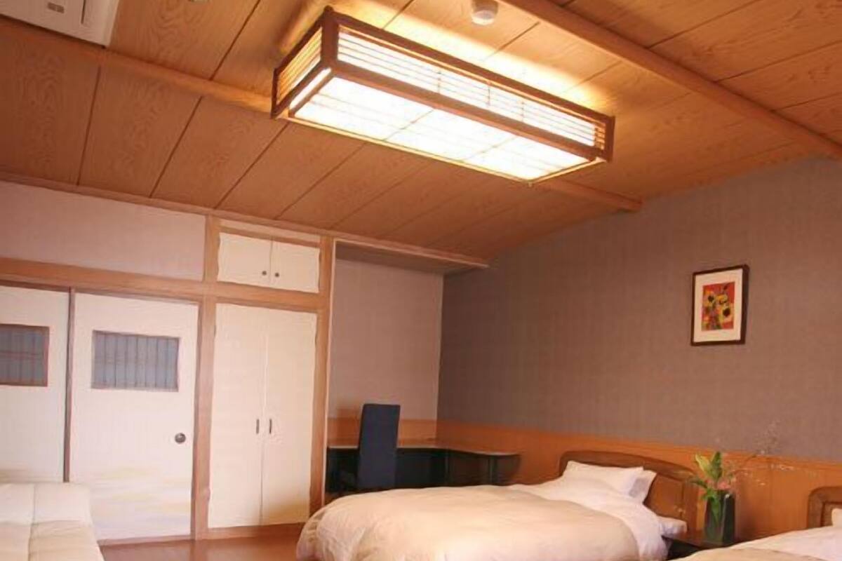 Quarto de hotel com duas camas, uma escrivaninha, uma cadeira e um guarda-roupa.