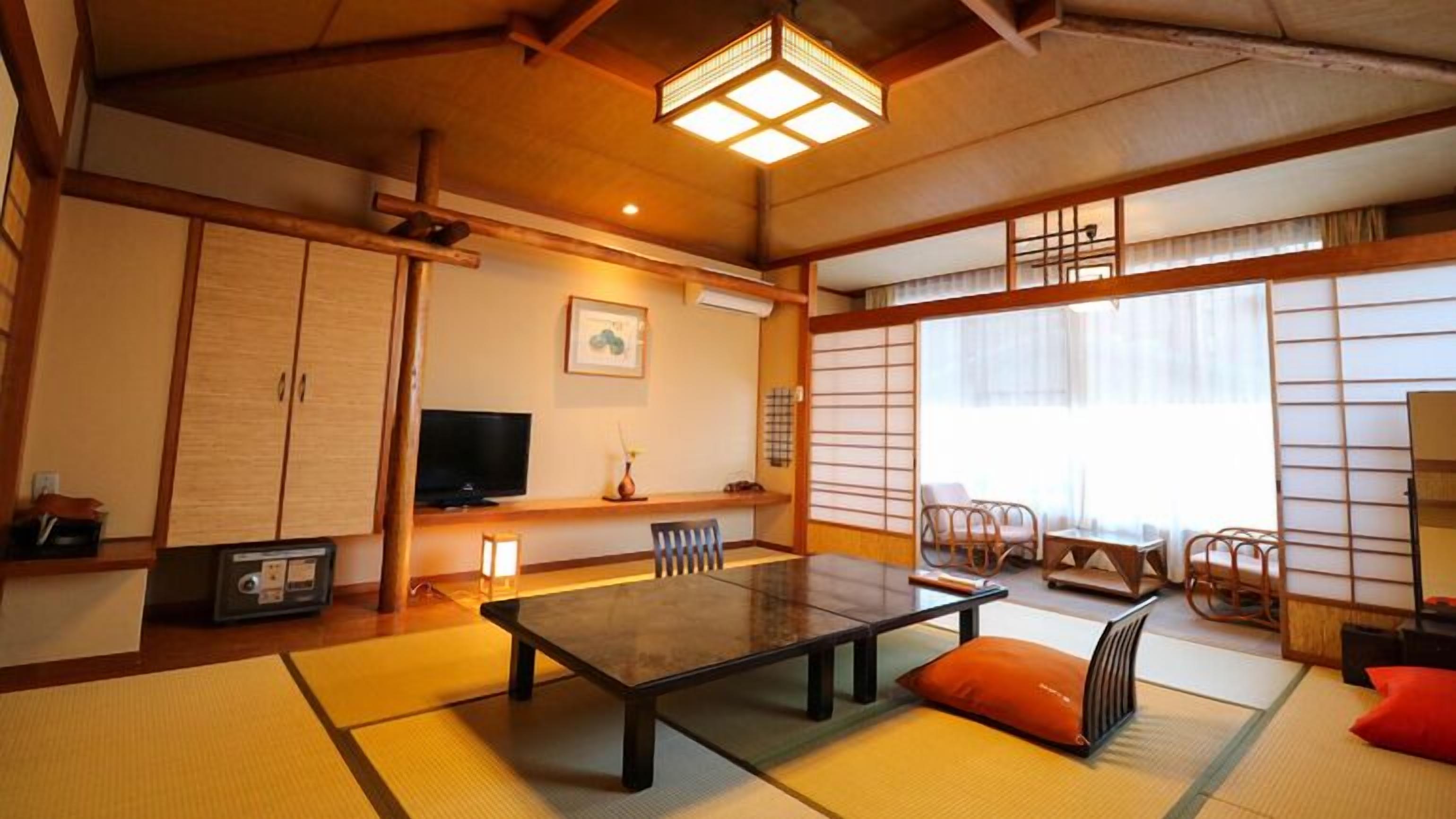 Um quarto japonês tradicional com tatames, uma mesa baixa, cadeiras, uma televisão e portas deslizantes.