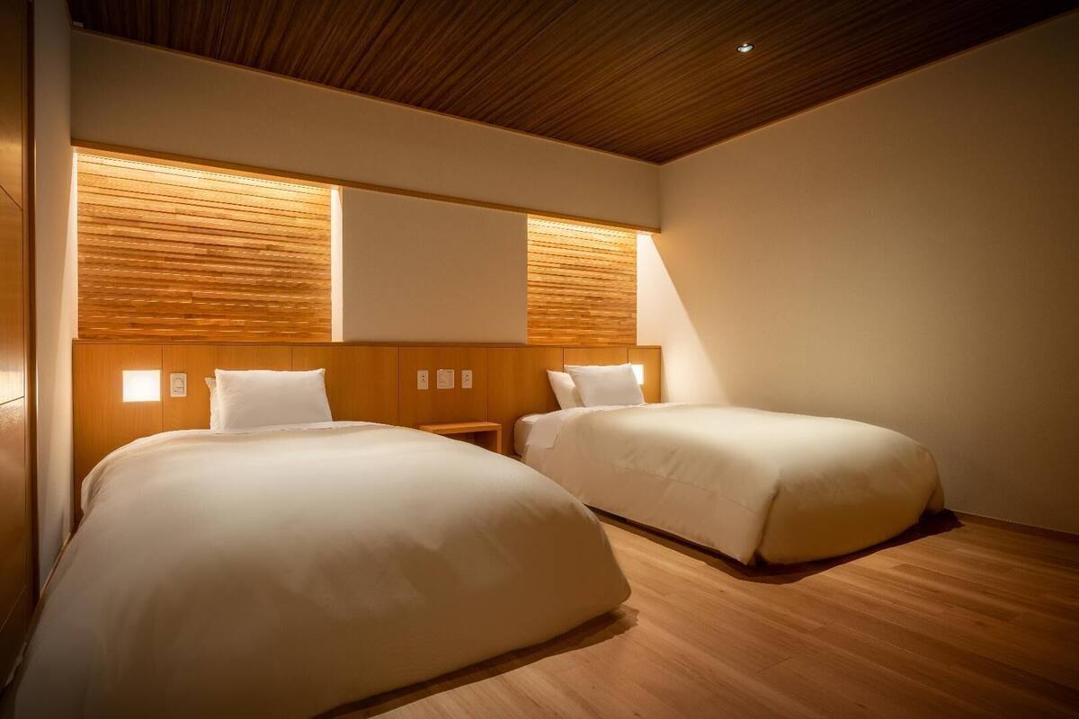 Quarto de hotel com duas camas e cabeceiras de madeira, além de teto inclinado.