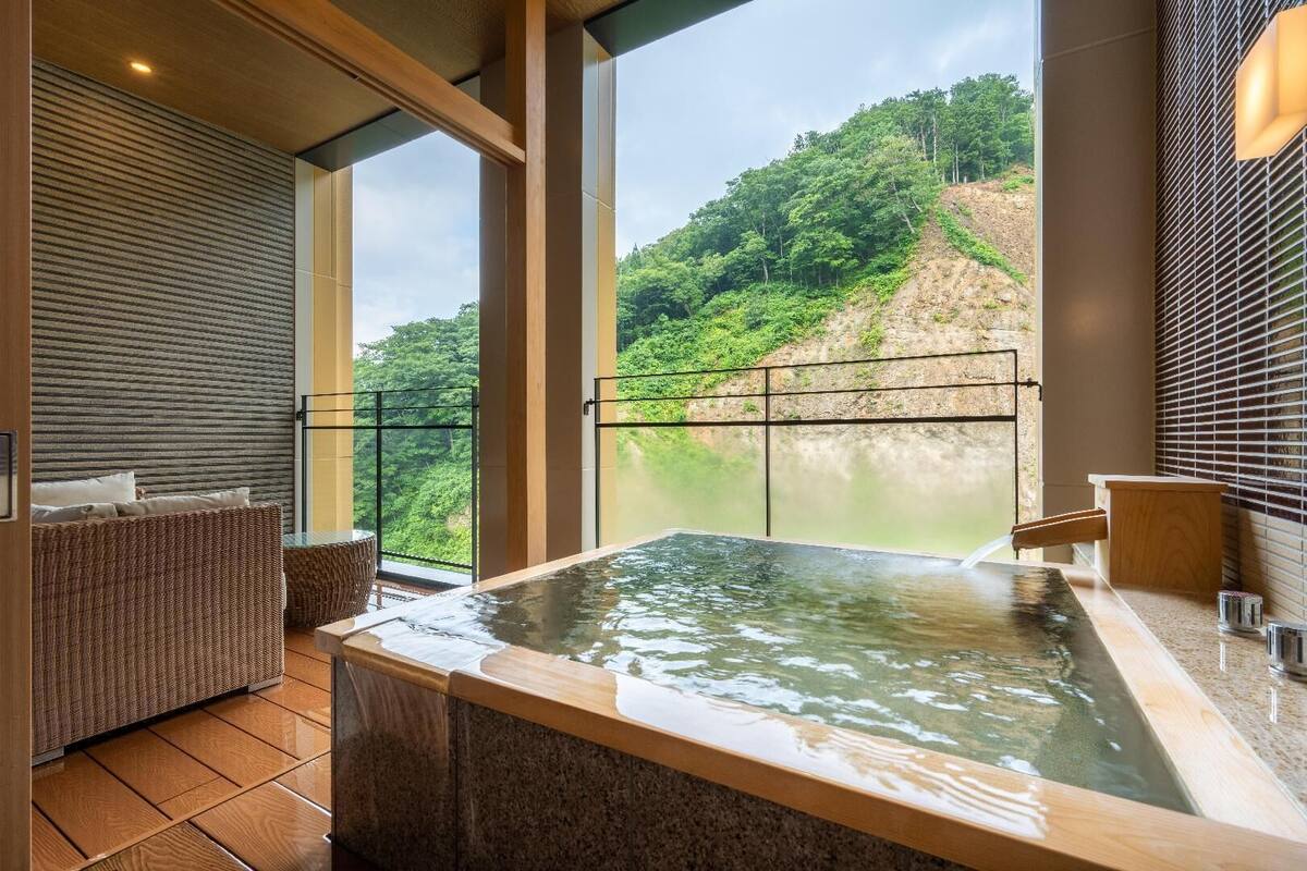 Uma área de spa com hidromassagem, móveis de vime e vista para uma encosta arborizada.