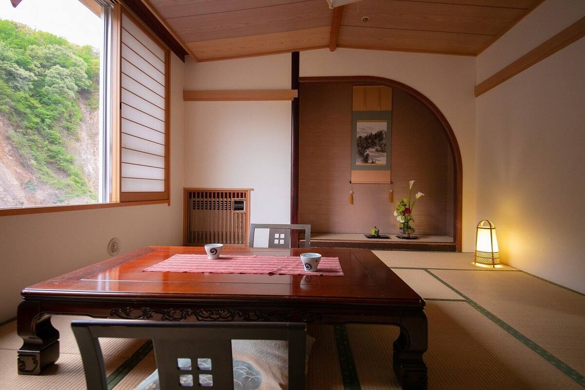 Um quarto japonês tradicional com tatames, uma mesa de madeira e uma porta deslizante que dá para uma vista de montanha.