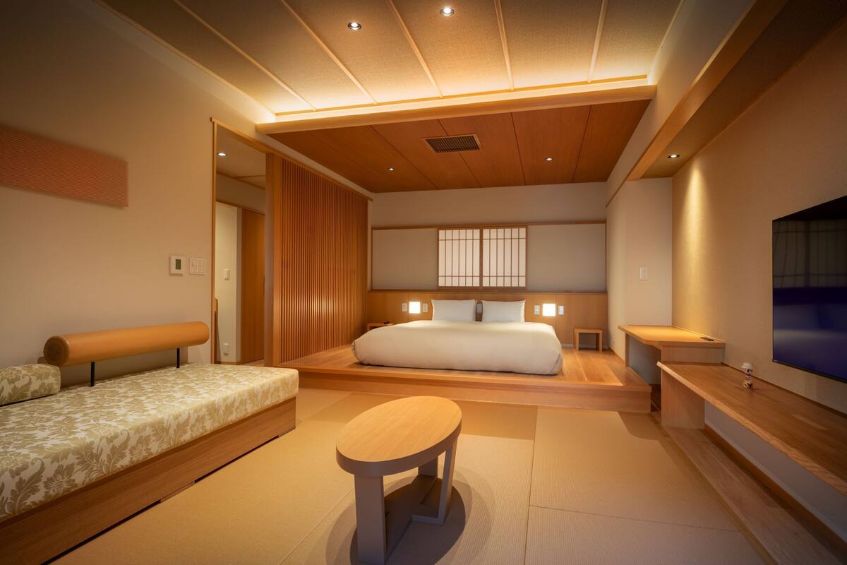 Quarto de hotel moderno com uma cama grande, um sofá, uma mesa pequena e uma televisão.