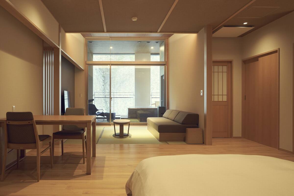 Quarto de hotel com cama, escrivaninha com cadeiras, sofá e varanda com vista.