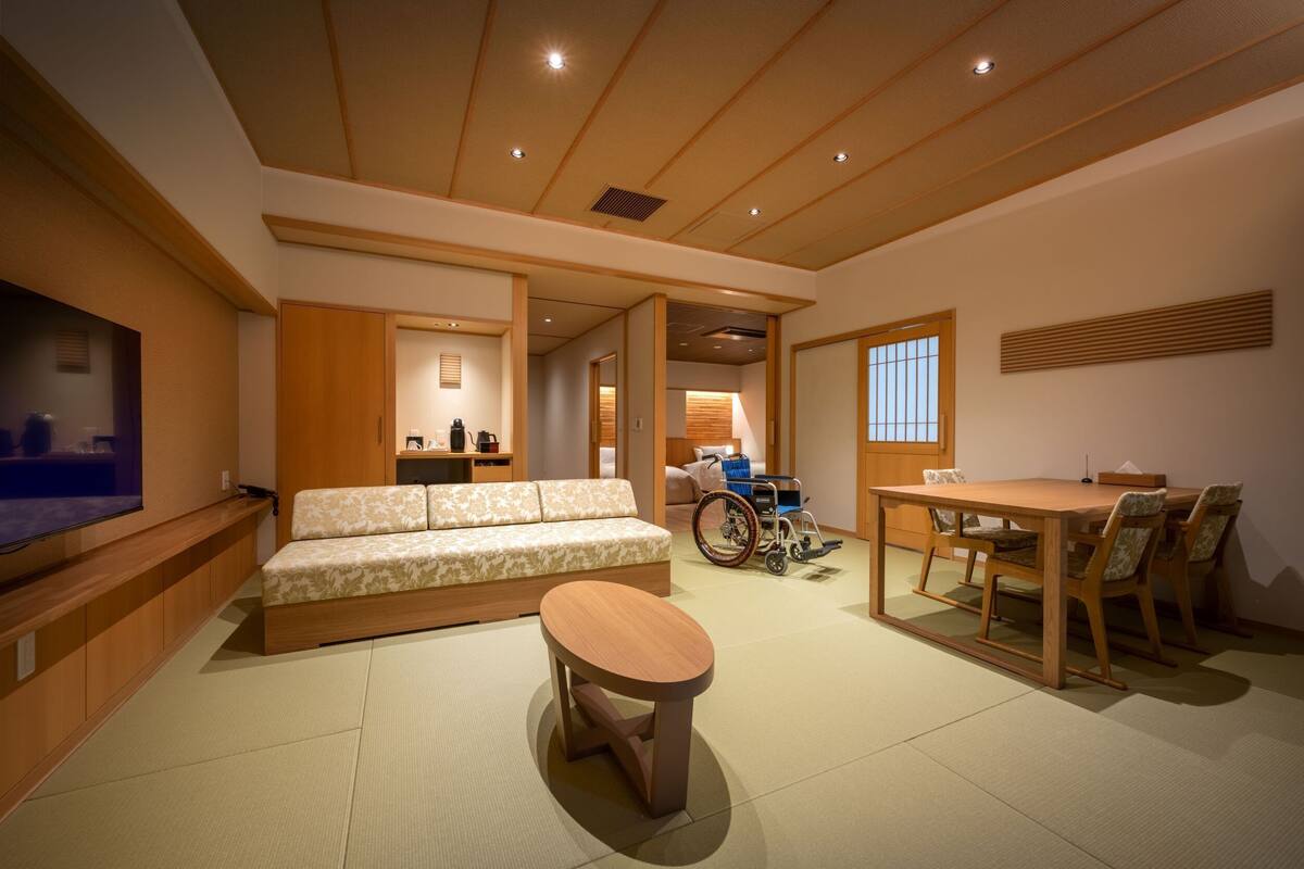 Quarto em estilo japonês tradicional com tatames, uma mesa de madeira baixa, um sofá e uma cadeira de rodas.