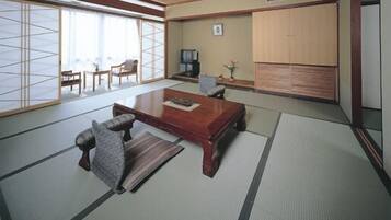 Um quarto japonês tradicional com esteiras de tatami, uma mesa de madeira baixa, um sofá e uma porta deslizante para uma varanda.