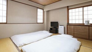 Quarto com duas camas, televisão e uma cozinha compacta.