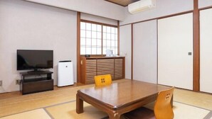 Quarto japonês tradicional com piso de tatame, uma mesinha, televisão e um refrigerador pequeno.