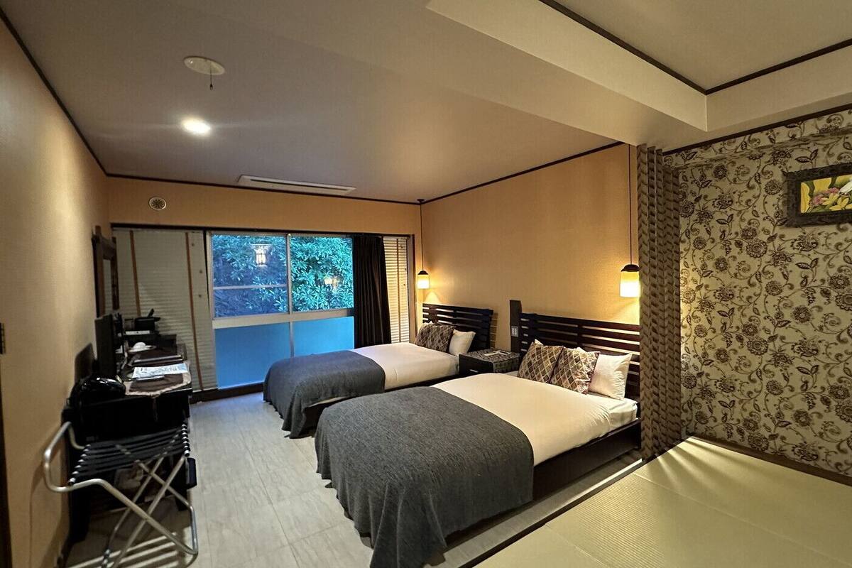 Quarto de hotel com duas camas, uma escrivaninha e vista para o verde lá fora.