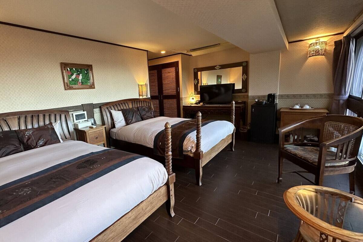 Quarto de hotel com duas camas, uma escrivaninha, uma cadeira e uma televisão.