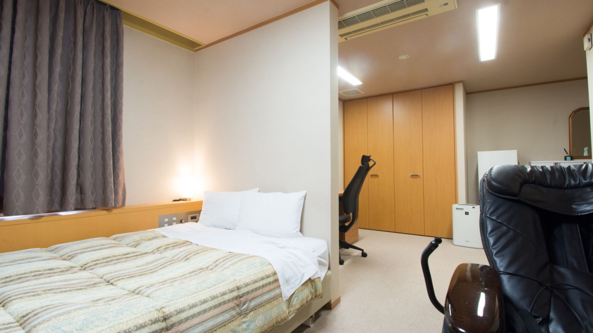 Quarto de hotel com cama, escrivaninha, cadeira, guarda-roupa e espelho.
