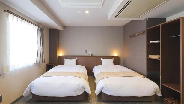 Quarto de hotel com duas camas, um guarda-roupa e uma mesa de cabeceira.