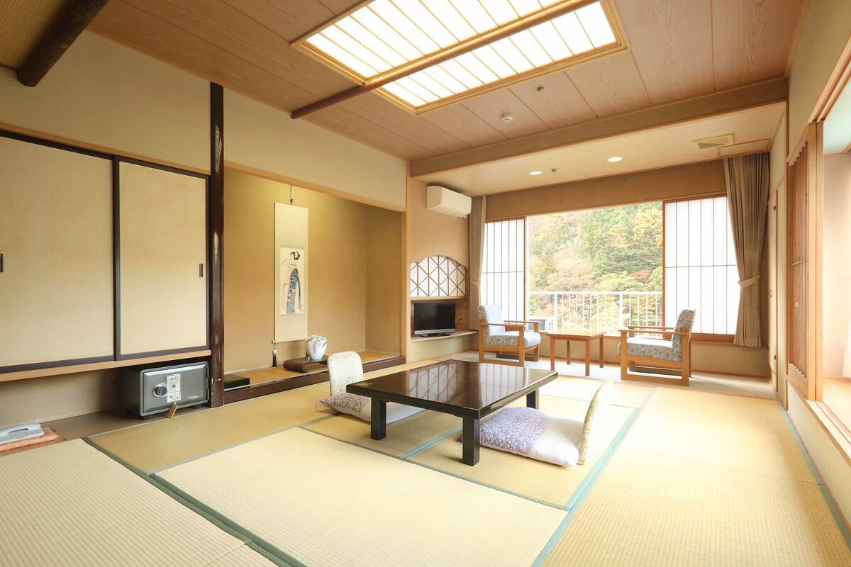 Um quarto japonês tradicional com tatame, uma mesa baixa e uma televisão.