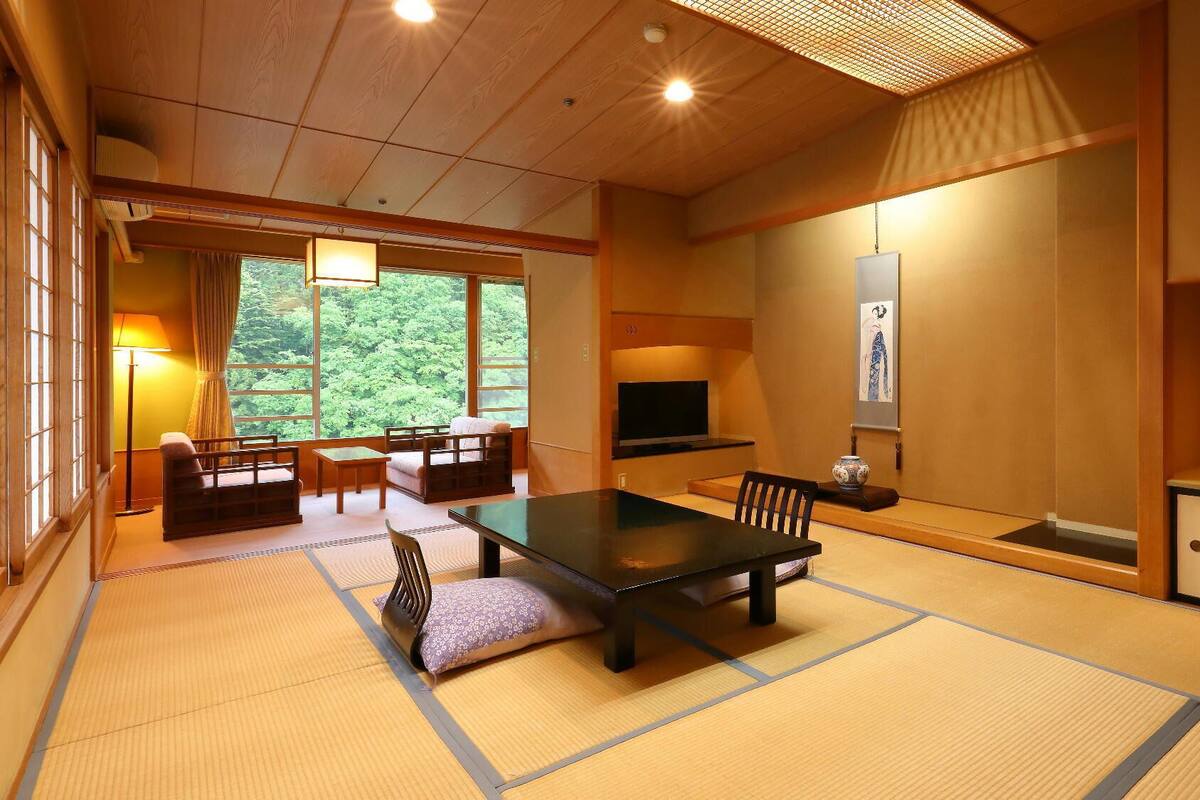 Um quarto japonês tradicional com tatames, uma mesa baixa, cadeiras, uma televisão e obras de arte nas paredes.