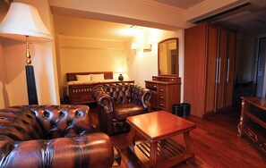 Quarto de hotel com sofá de couro, mesa de madeira, cama com cabeceira, cômoda e espelho.