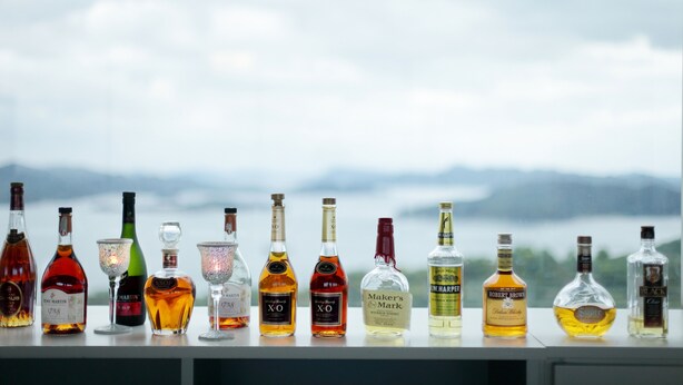 Várias garrafas de bebidas alcoólicas dispostas numa estante, com uma paisagem montanhosa ao fundo.