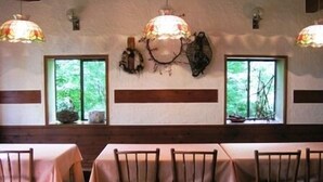 Uma sala de jantar com mesas e cadeiras, janelas amplas com vista para o verde e decoração nas paredes.