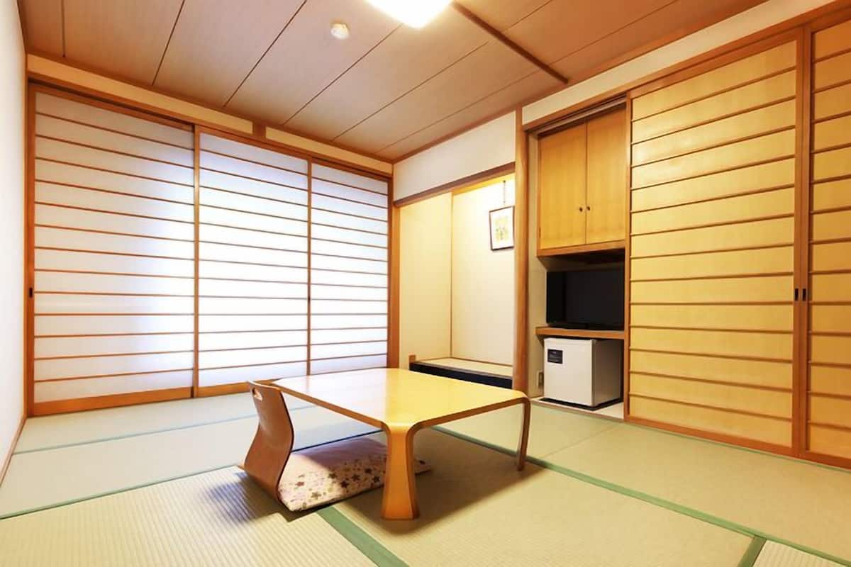 Um quarto japonês tradicional com tatames, uma mesa baixa, portas deslizantes e uma televisão.