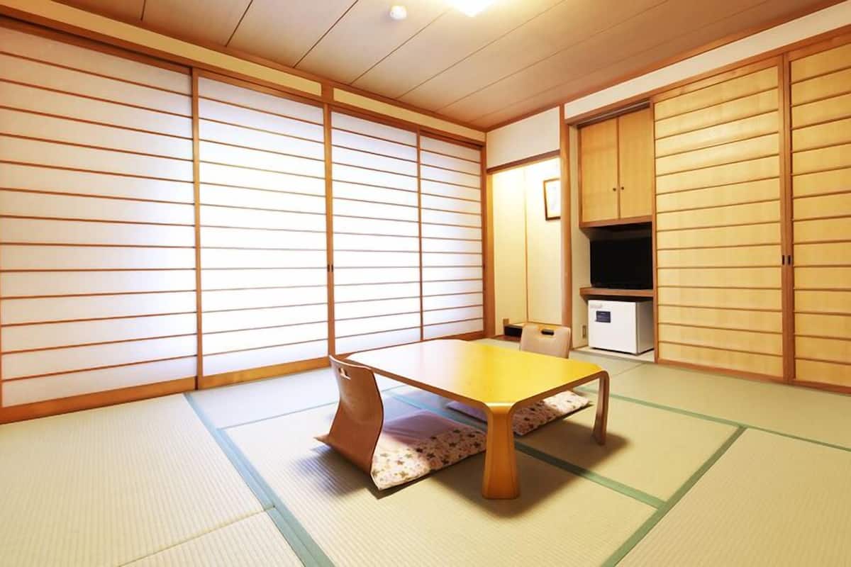 Um quarto japonês tradicional com tatames, uma mesa baixa, portas deslizantes e um armário embutido para a televisão.