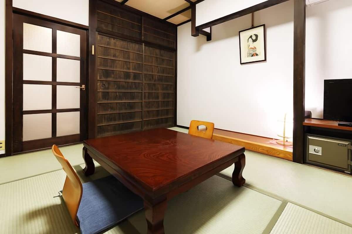 Um quarto japonês tradicional com tatames, uma mesa de madeira baixa e uma televisão.