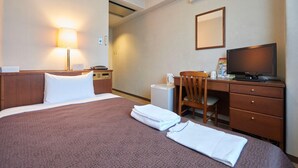 Quarto de hotel com cama, escrivaninha, cadeira, televisão e luminária.
