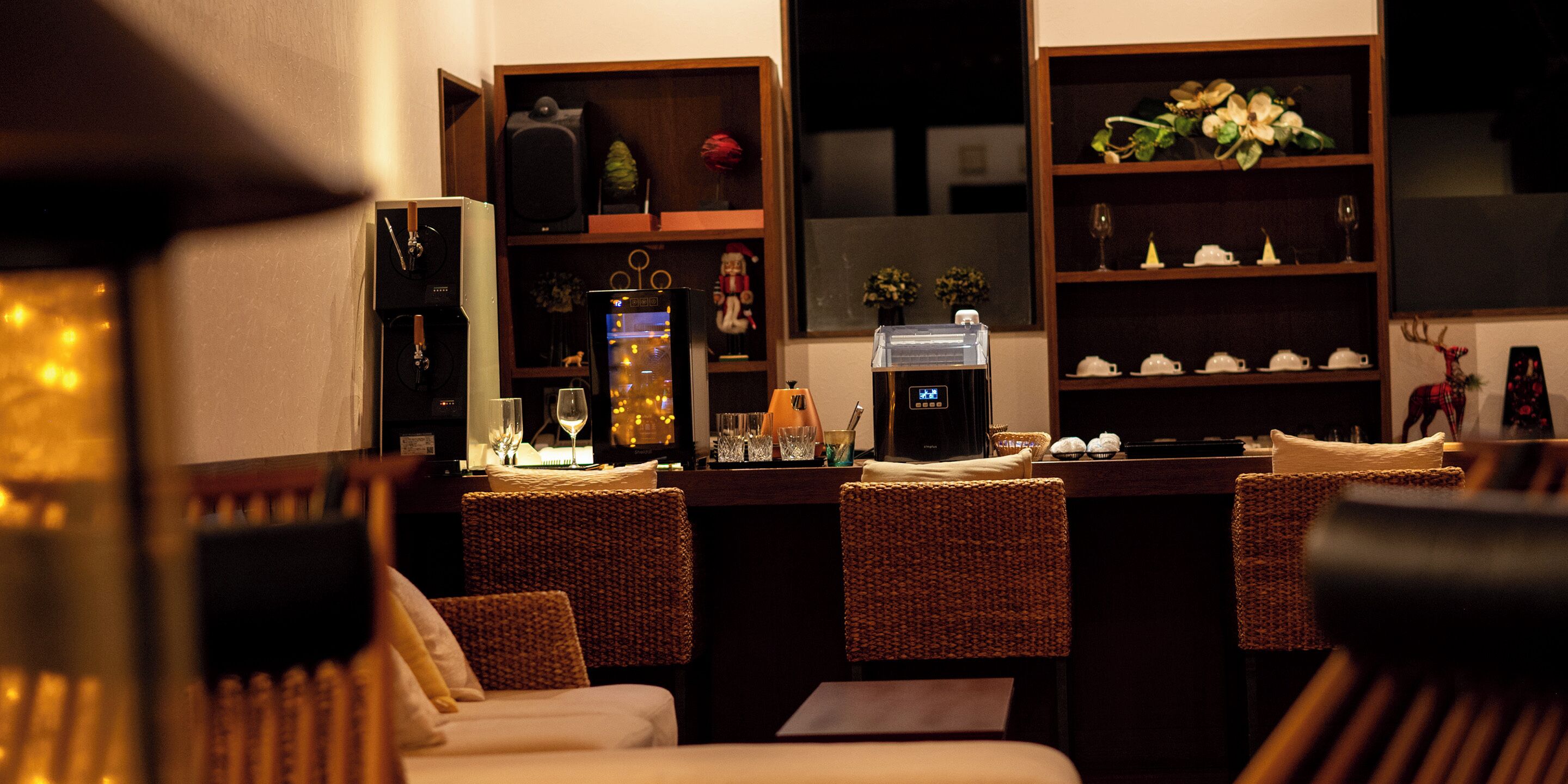 Uma área de bar com mobiliário de vime, prateleiras com objetos decorativos e uma máquina de café.