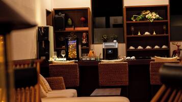 Uma área de bar com mobiliário de vime, prateleiras com objetos decorativos e uma máquina de café.