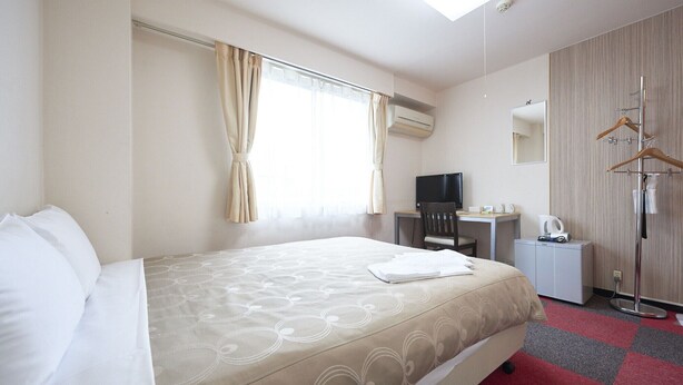 Quarto de hotel com cama, uma secretária com cadeira, televisão e guarda-roupa.