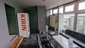 Quarto com um minibar branco com a marca 'KIRIN', um extintor de incêndio, uma lixeira e uma janela com vista para edifícios.