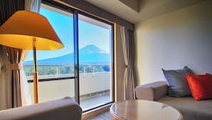Quarto de hotel com sofá, uma pequena mesa e uma luminária. Há uma janela grande com vista para uma montanha.
