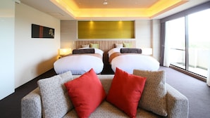 Quarto de hotel com duas camas, um sofá e uma janela grande.