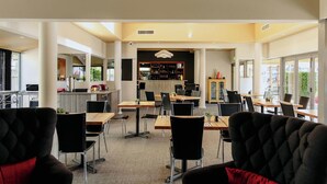 Uma sala de jantar de hotel com várias mesas e cadeiras, um bar e vista para o exterior.