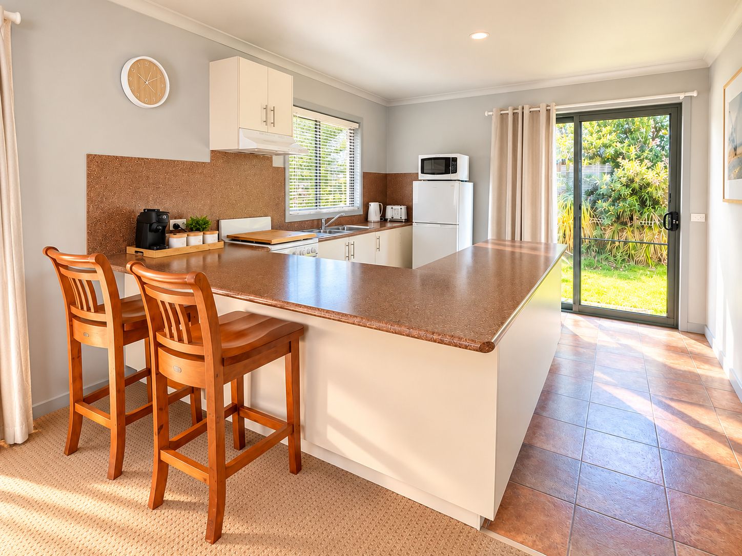 Cozinha moderna com ilha central, banquetas, micro-ondas e porta de vidro deslizante para um jardim.