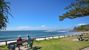 Um banco com vista para a praia e o oceano, com uma área ajardinada e um corrimão de madeira.