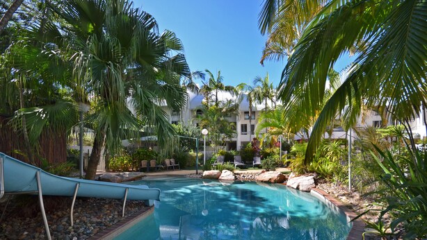 Uma piscina cercada por palmeiras e cadeiras de lounge, com um edifício ao fundo.