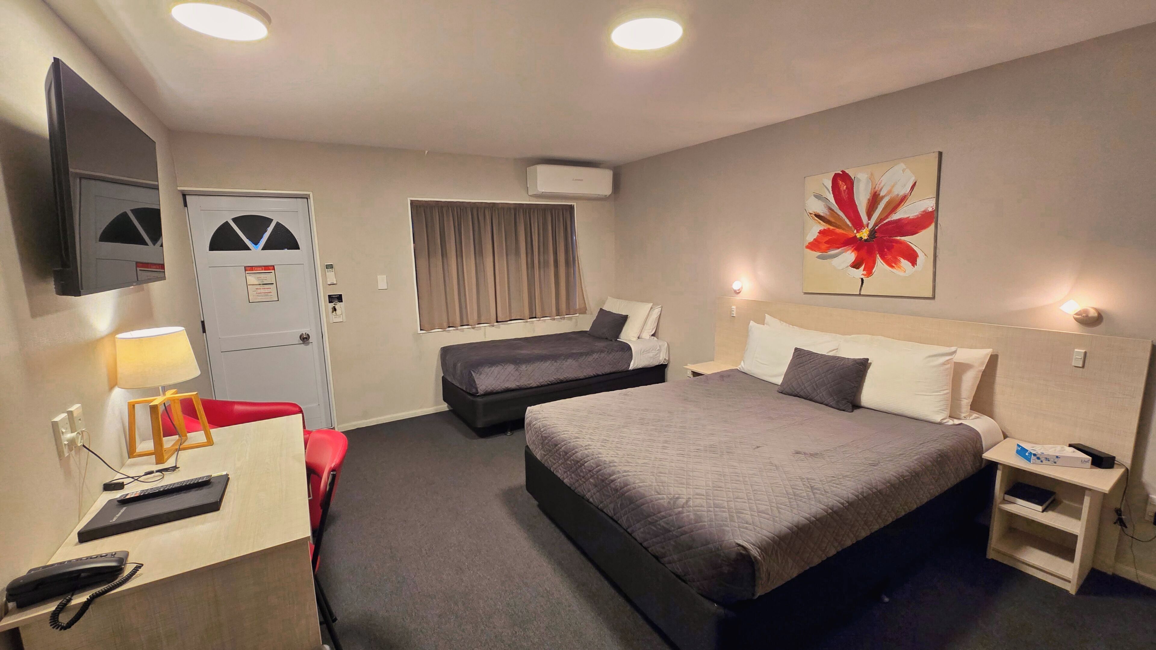Quarto de hotel com duas camas, uma mesa com telefone, uma luminária e um quadro de flor na parede.