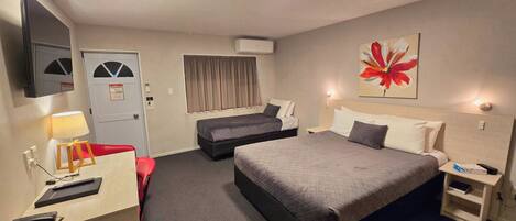 Quarto de hotel com duas camas, uma mesa com telefone, uma luminária e um quadro de flor na parede.