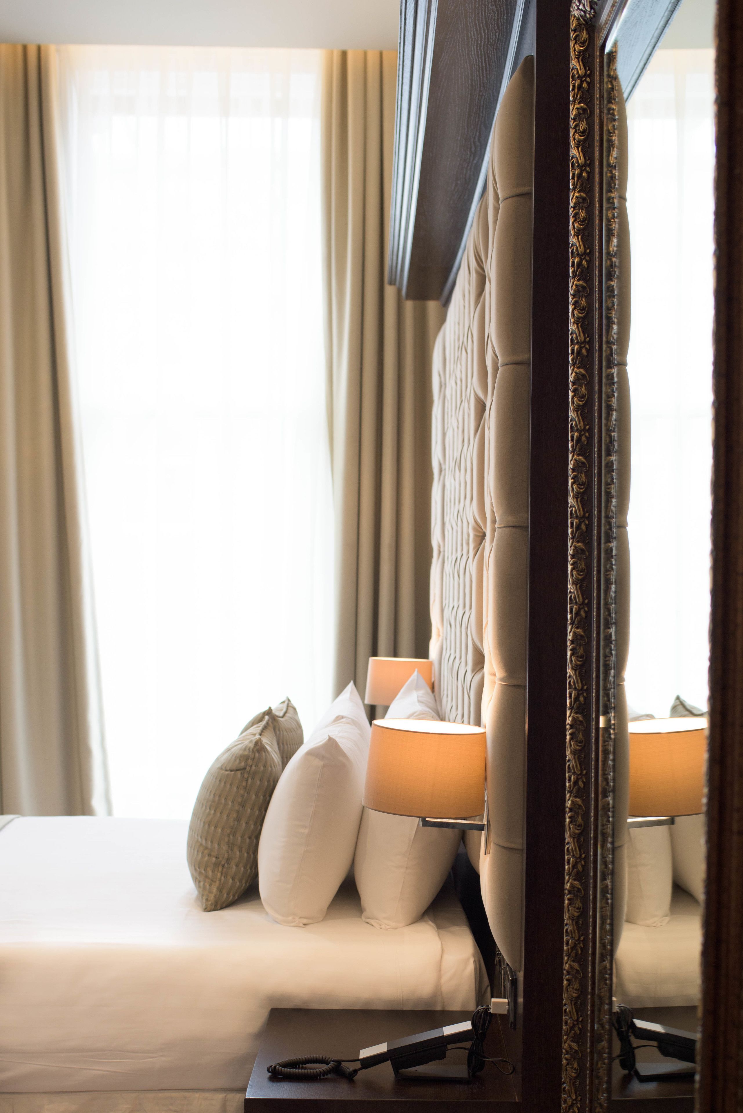 Quarto de hotel com cama, almofadas, luminária e espelho.