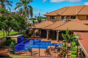 Um edifício de dois andares com piscina, área de estar externa e varanda coberta.