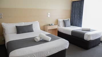 Quarto de hotel com duas camas, uma mesa de cabeceira e uma janela com cortinas.