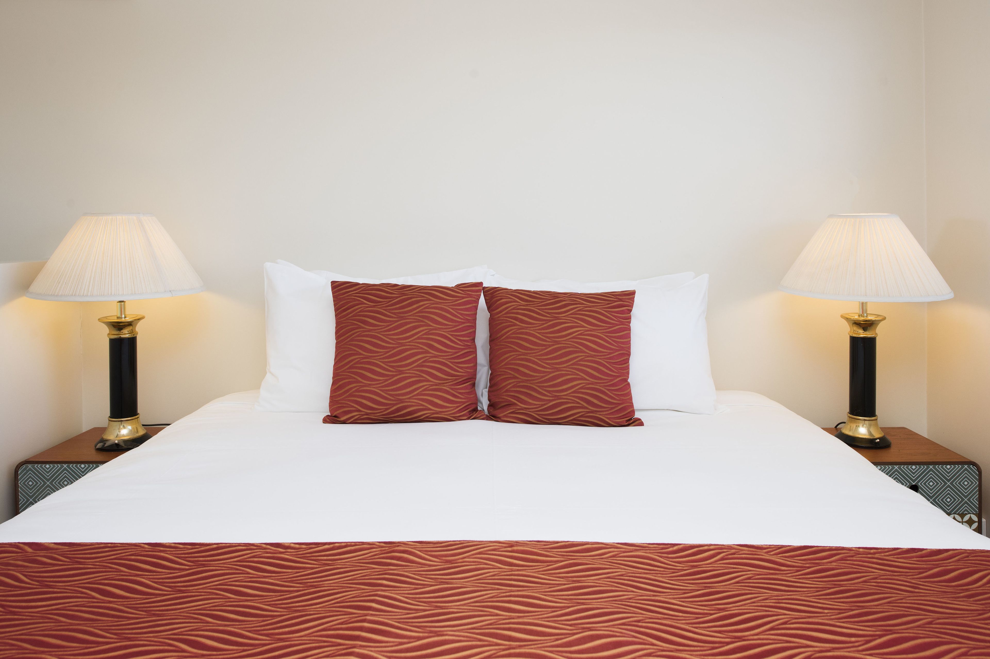 Cama bem arrumada com duas almofadas, duas luminárias de cabeceira e um cobreleite estampado.