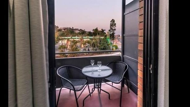 Varanda com duas cadeiras e uma mesa, com vista para um horizonte urbano com edifícios e áreas verdes.