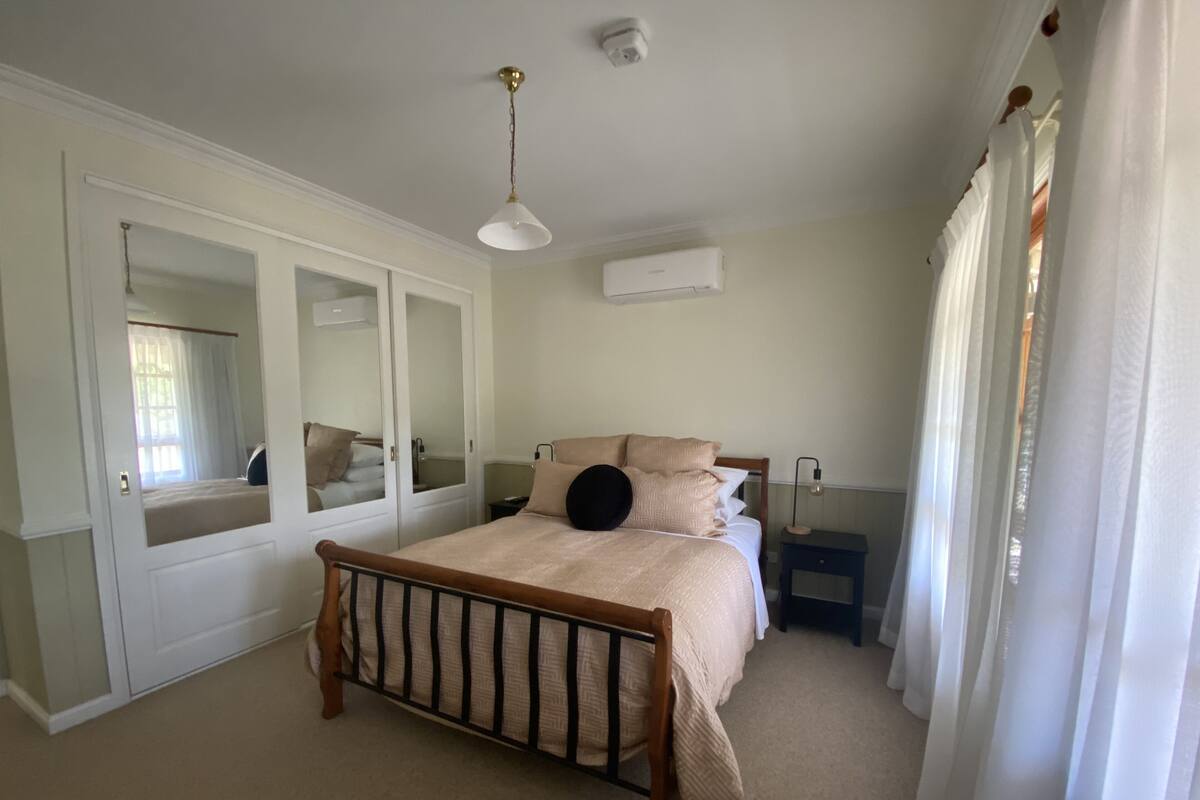 Quarto com cama de madeira, mesa de cabeceira, luminária, ar condicionado e espelho.
