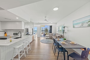 Cozinha moderna com armários brancos, uma ilha central com banquetas e uma área de jantar com mesa posta para quatro.