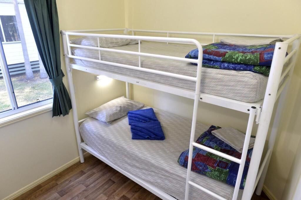 Uma cama beliche com dois níveis, uma janela com cortinas e piso de madeira.